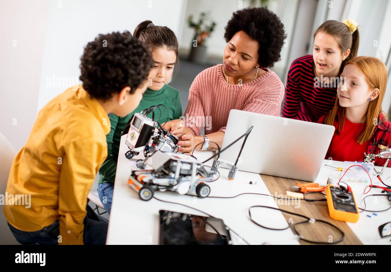 Group of happy kids with their African American female science teacher with laptop programming ...