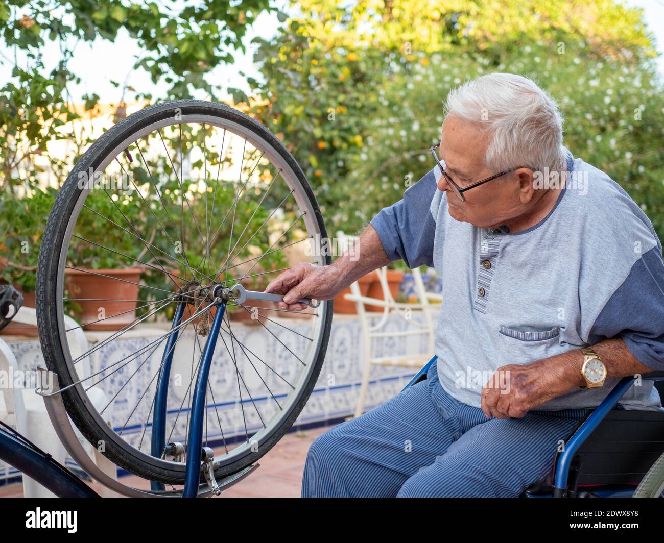 An old man in a wheelchair fixing a bicycle tire Stock Photo - Alamy