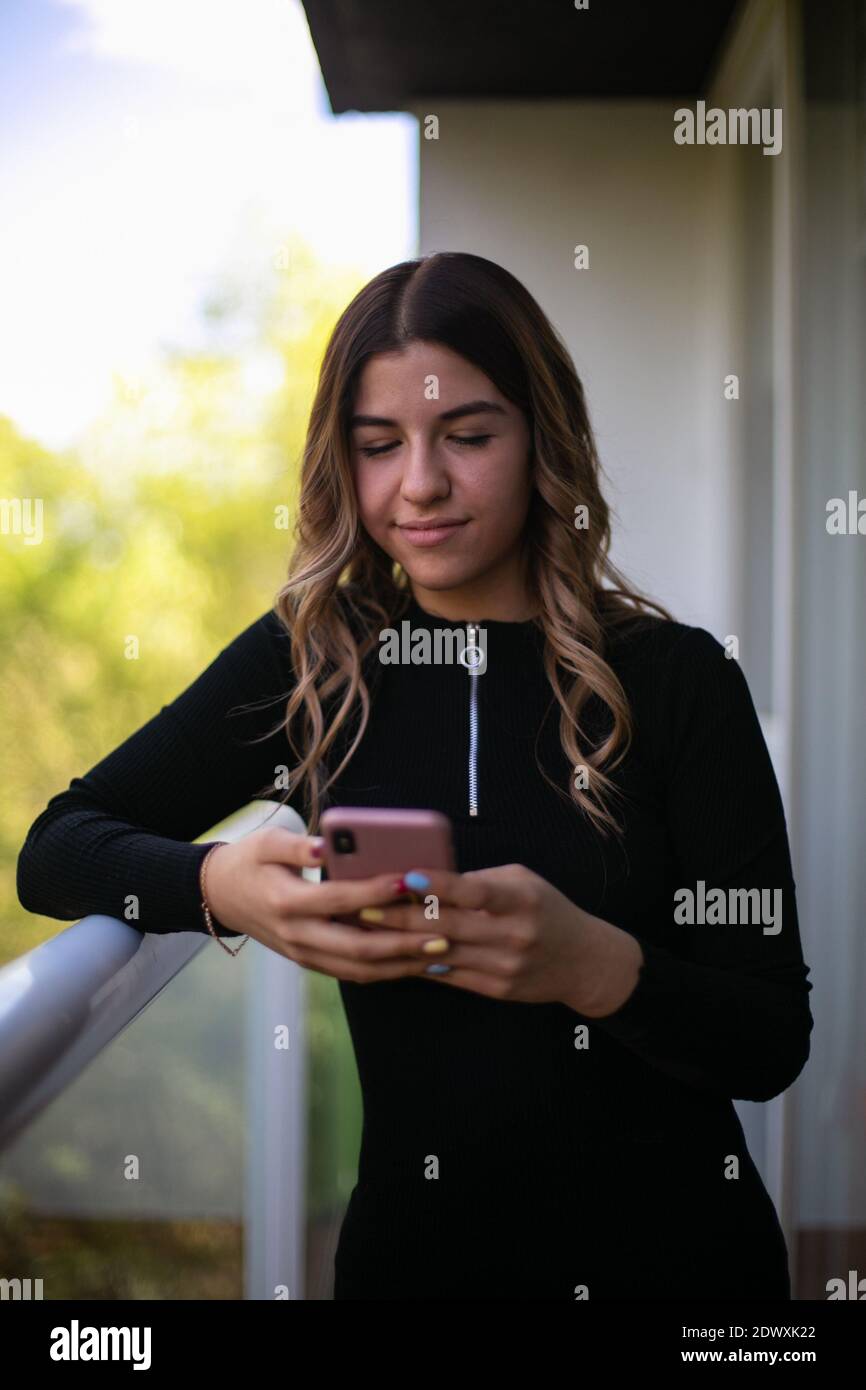 Young woman standing alone outside and sending a text message on her ...