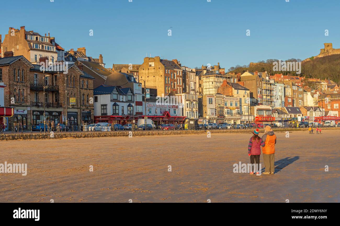 Beach and town in winter. Two people standing on a deserted beach look ...