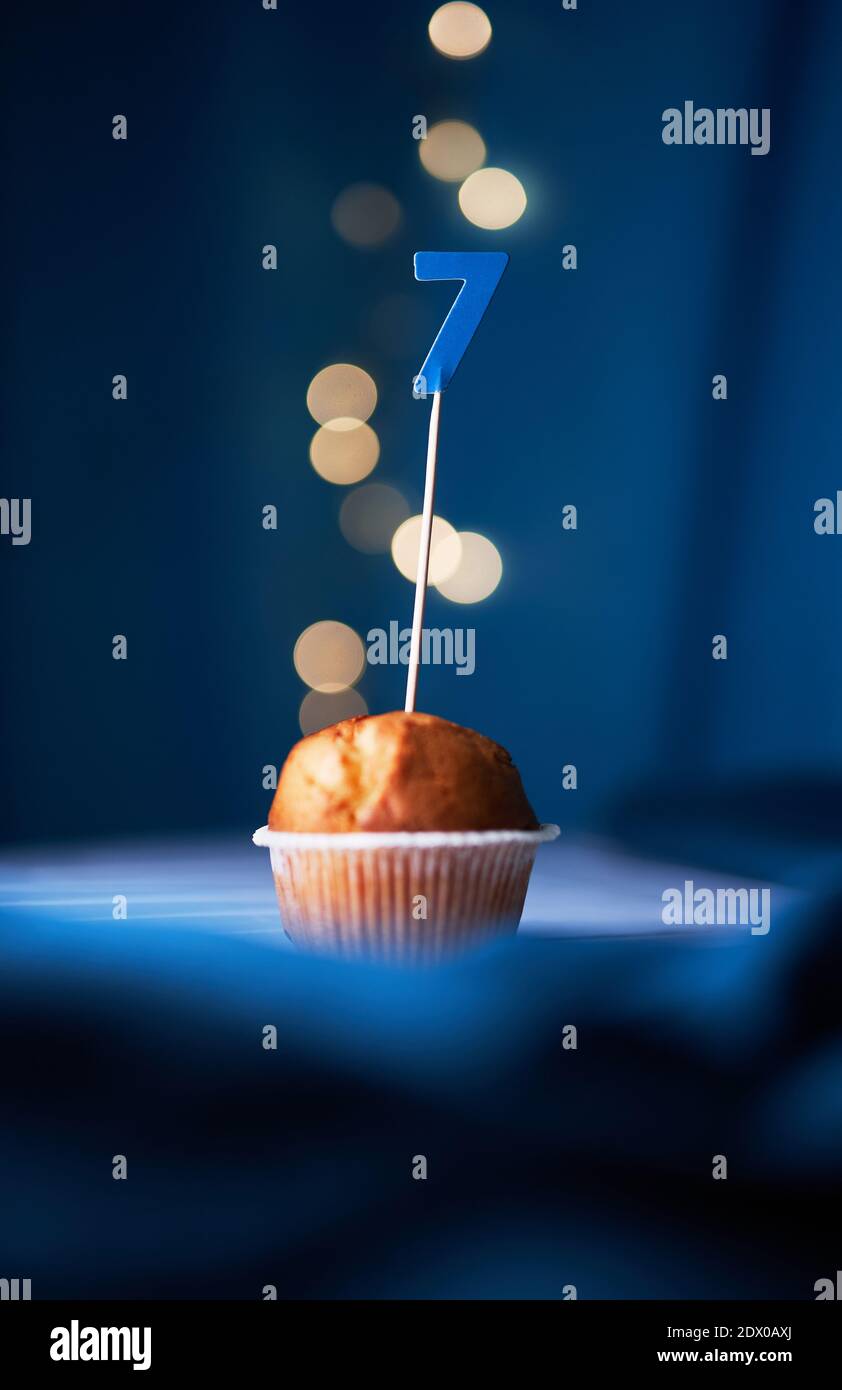 Birthday cupcake or muffin with number seven (7) and blurred lights on ...