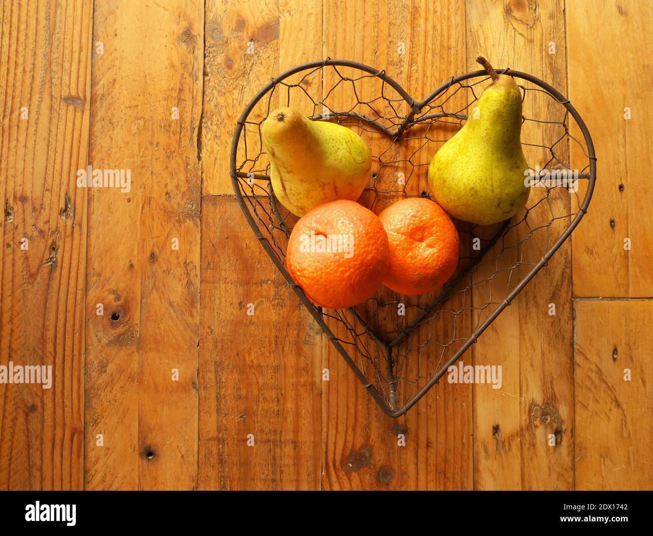 Picture of three pears and two clementines inside a heart-shaped basket ...