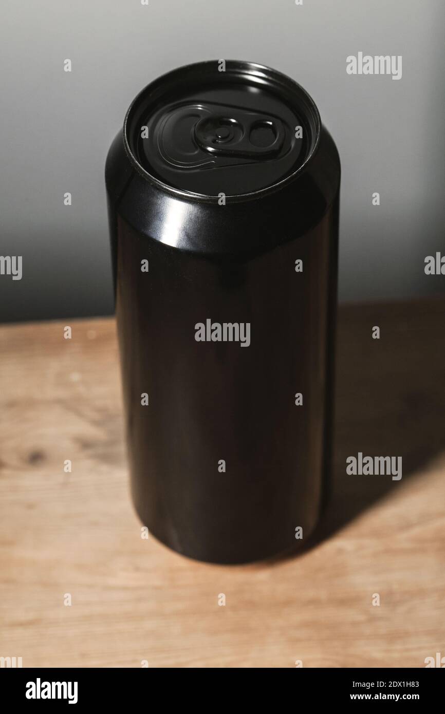Closed shiny black aluminum can stands on a wooden table, standard soft ...