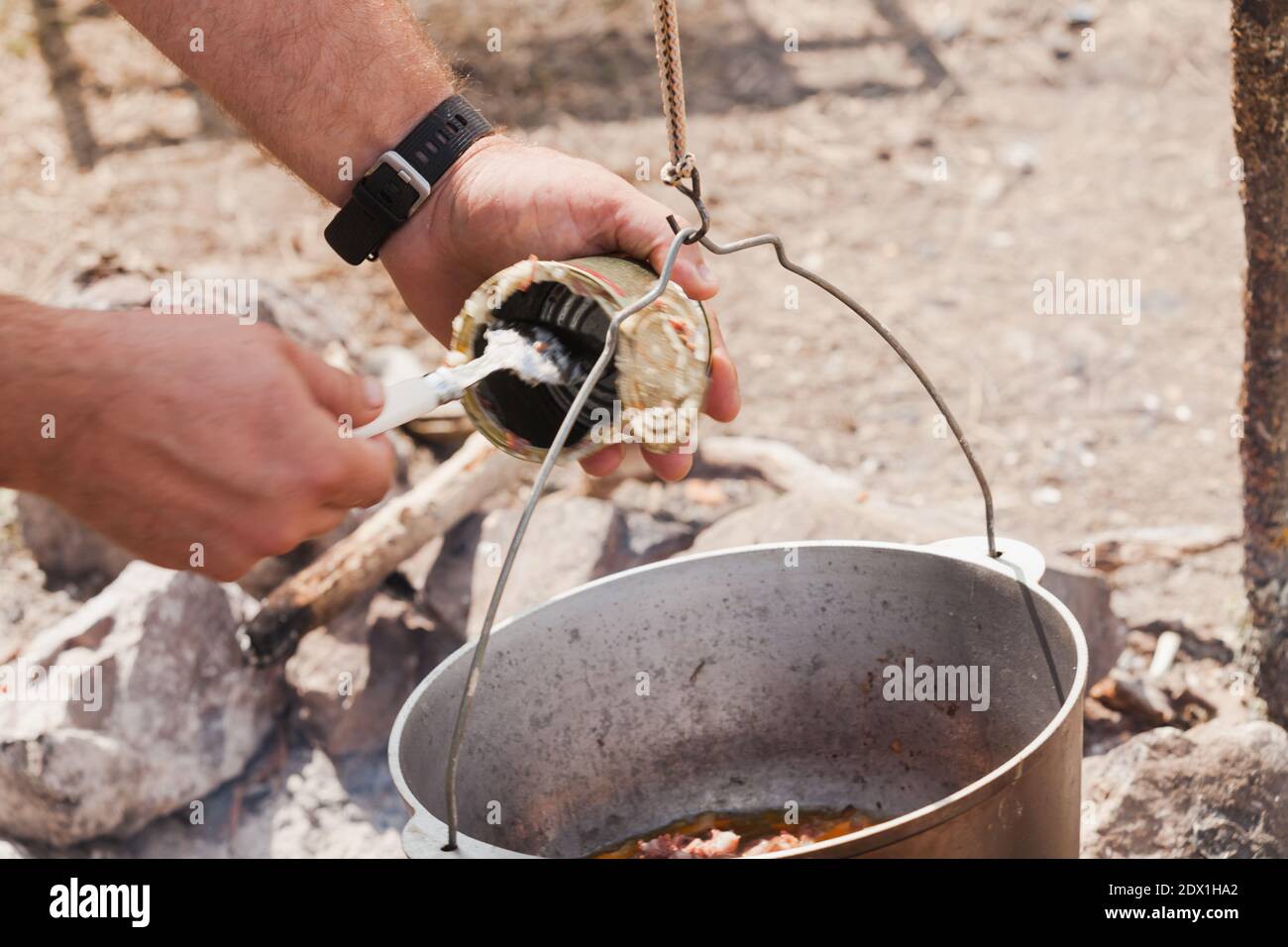 Adding a beef stew to a soup in a cauldron, camping meal preparing on ...