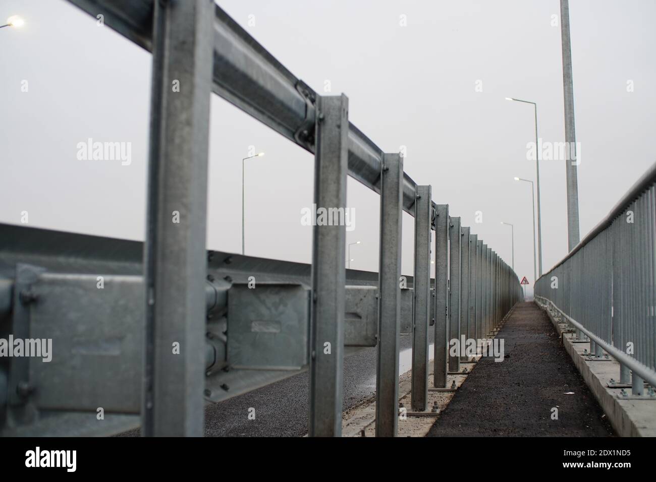 A view of a narrow sidewalk bridge lined with metal railings Stock ...
