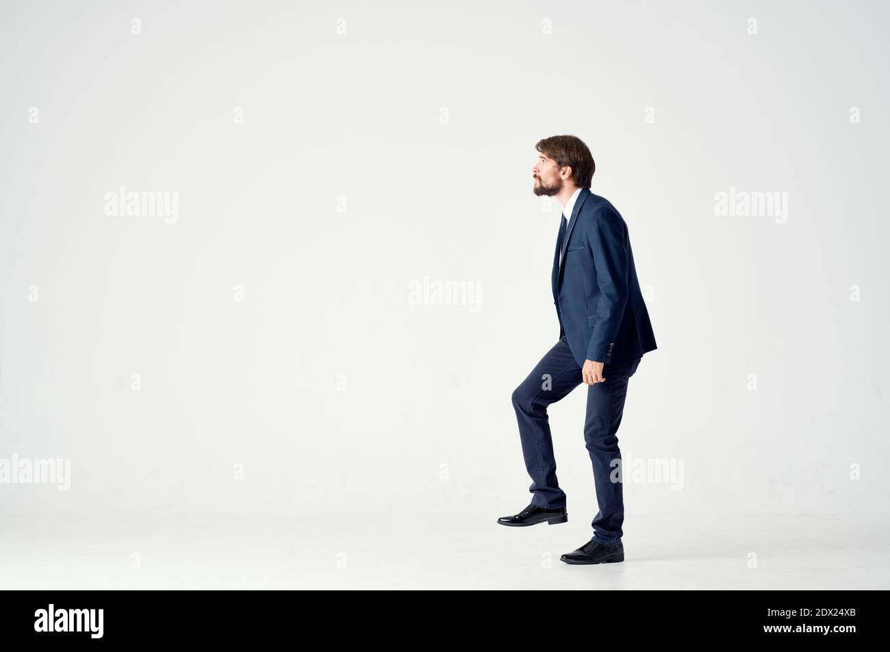business man in a blue suit stands on one leg on a light background ...