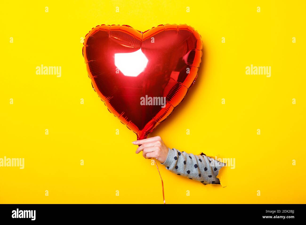 Female hand in a torn yellow background holding an air inflatable red ...