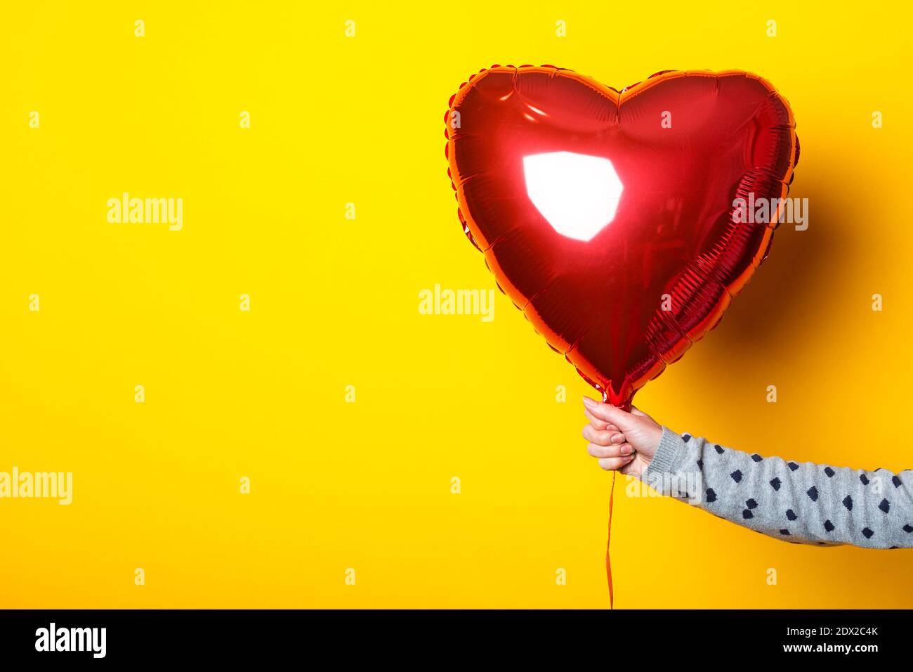 Female hand holds an inflatable heart-shaped balloon on a yellow ...