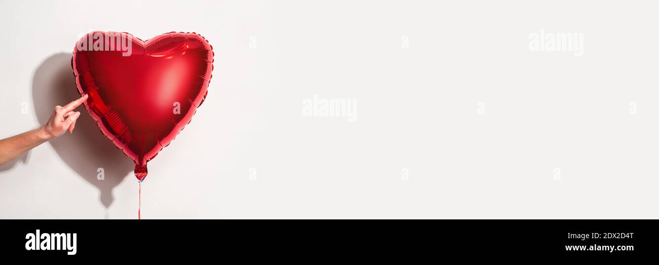 female hand points a finger at a red air balloon in the form of a heart ...