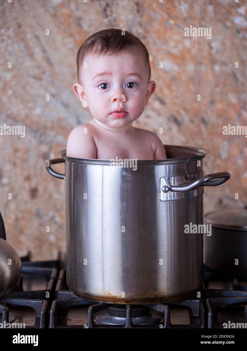 Cute Baby boy sitting in stainless steel pot colander in the kitchen ...
