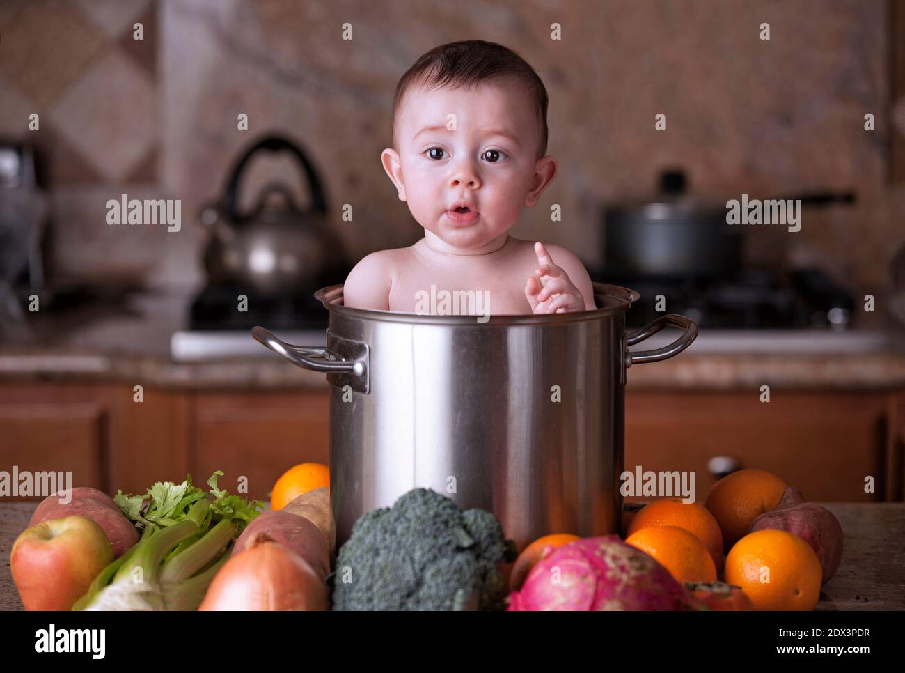 Cute Baby boy sitting in stainless steel pot colander in the kitchen ...