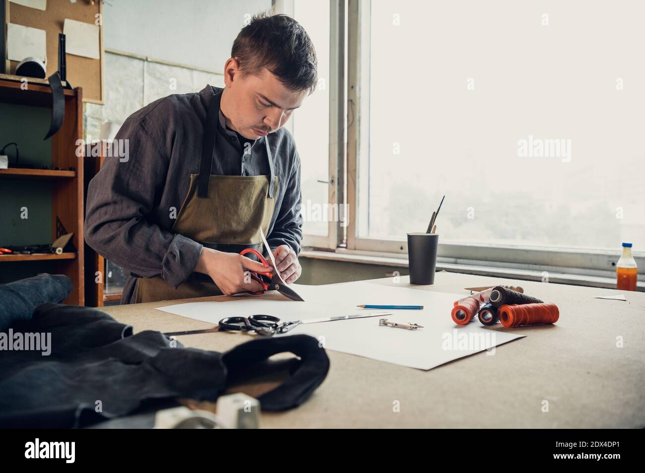 A young shoemaker makes a drawing for a pattern for leather shoes on a ...