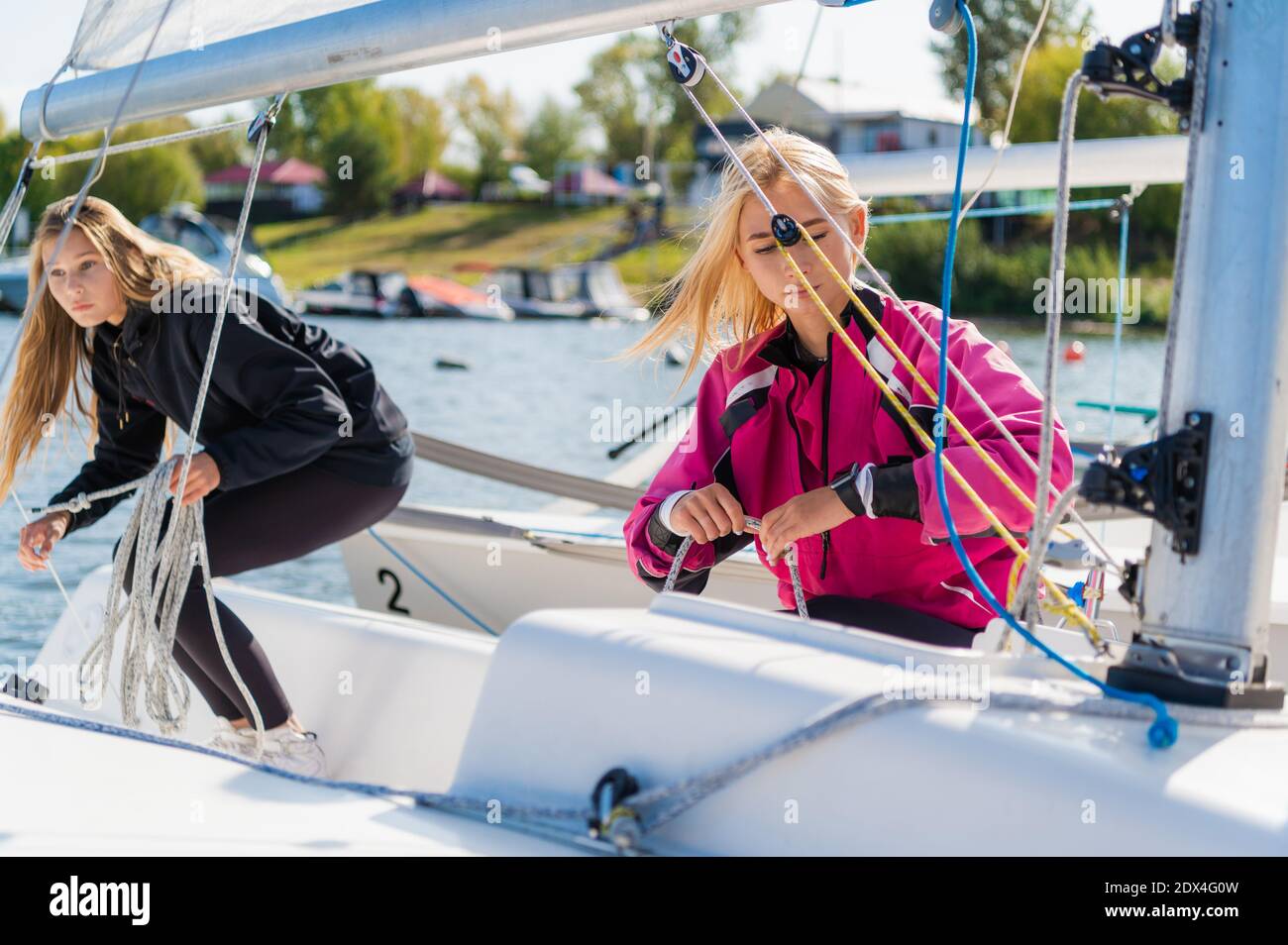 On the pier, two pretty girls pull sails on a boat to participate in a ...
