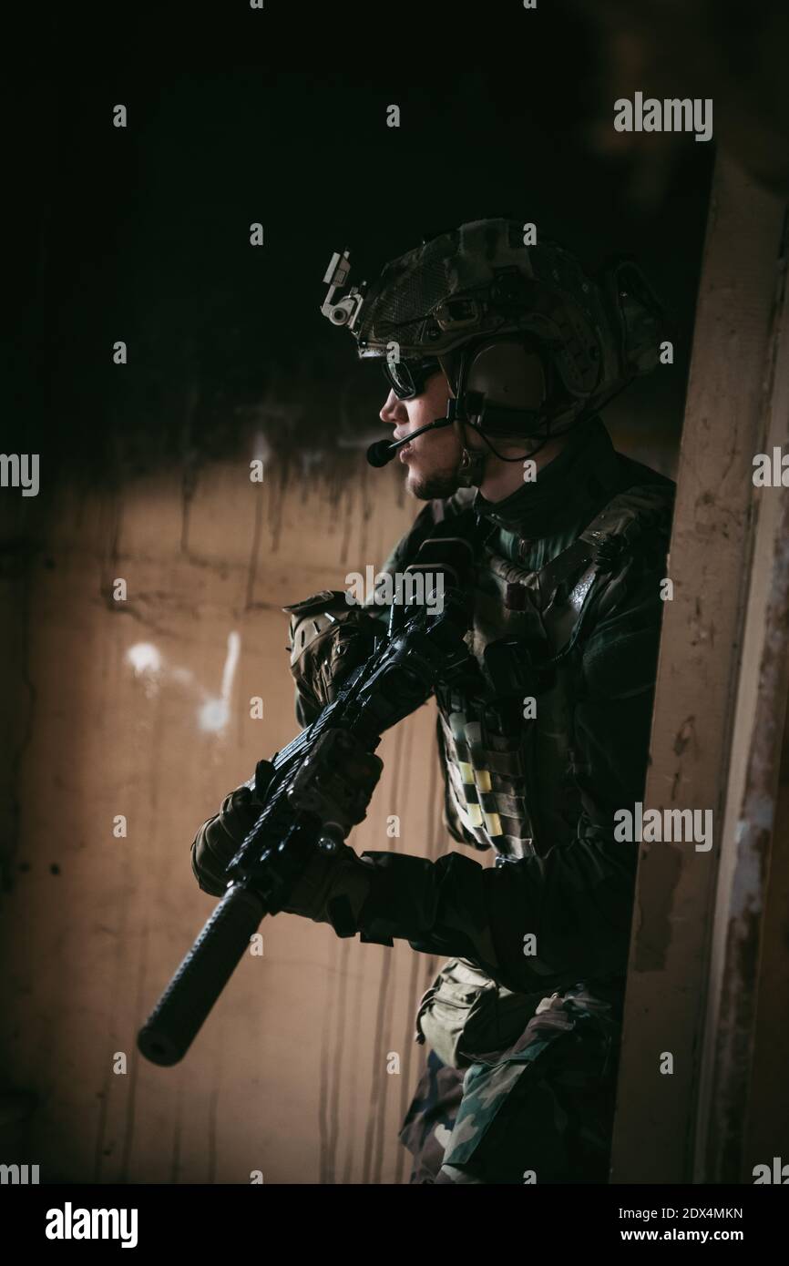 Military man with assault rifle standing inside building, he is ready ...