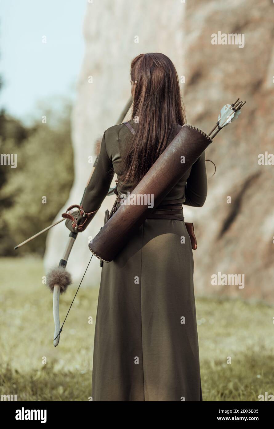 Woman archer with arrows on her back, stands with her back to the ...