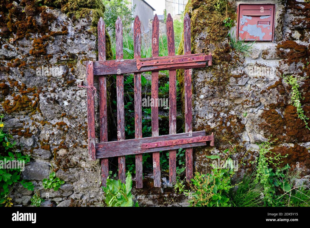 old wood red gate, with crooked pieces, closed between two rock walls ...