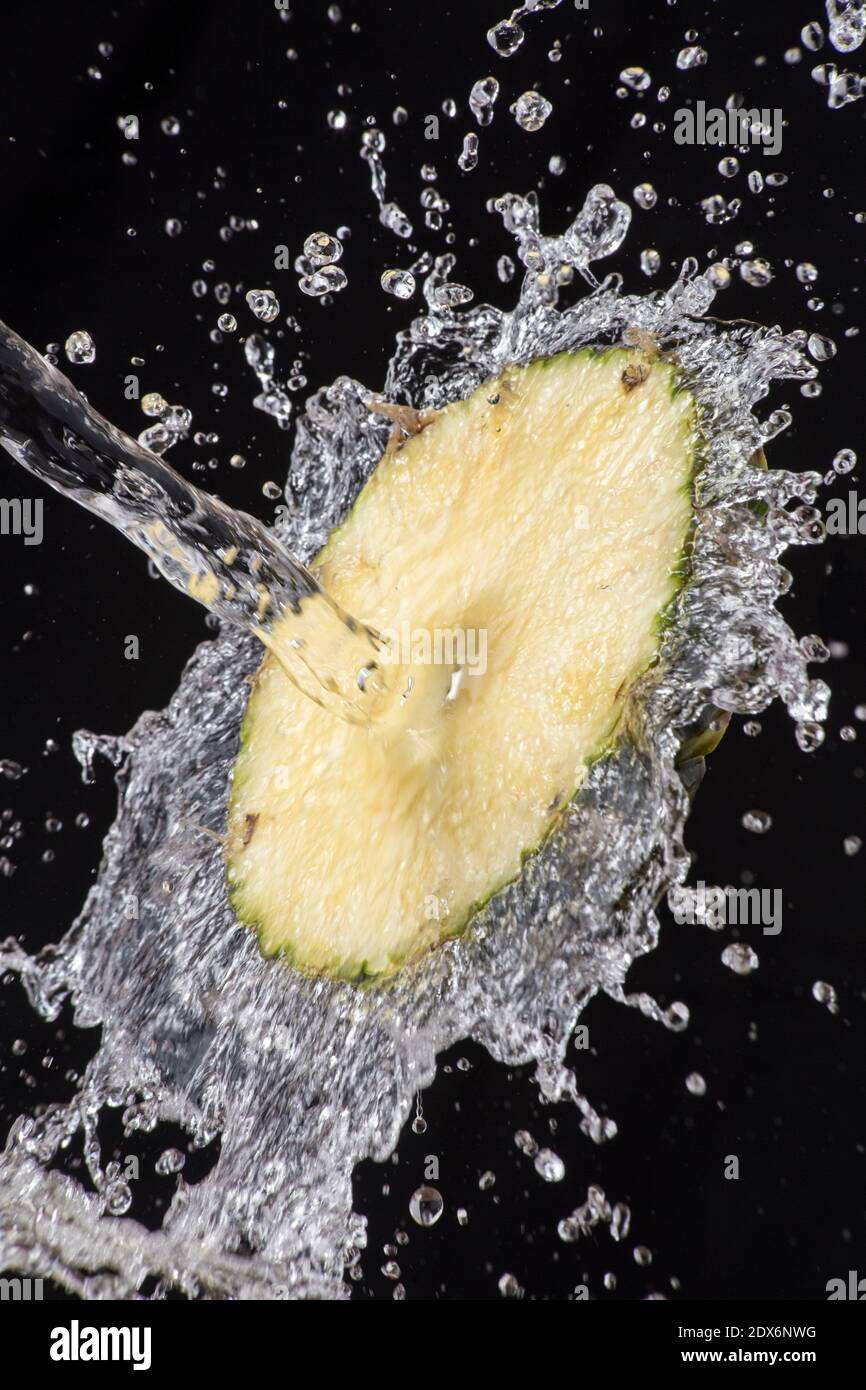 A slice of fresh pineapple splashed by a jet of water. black background ...