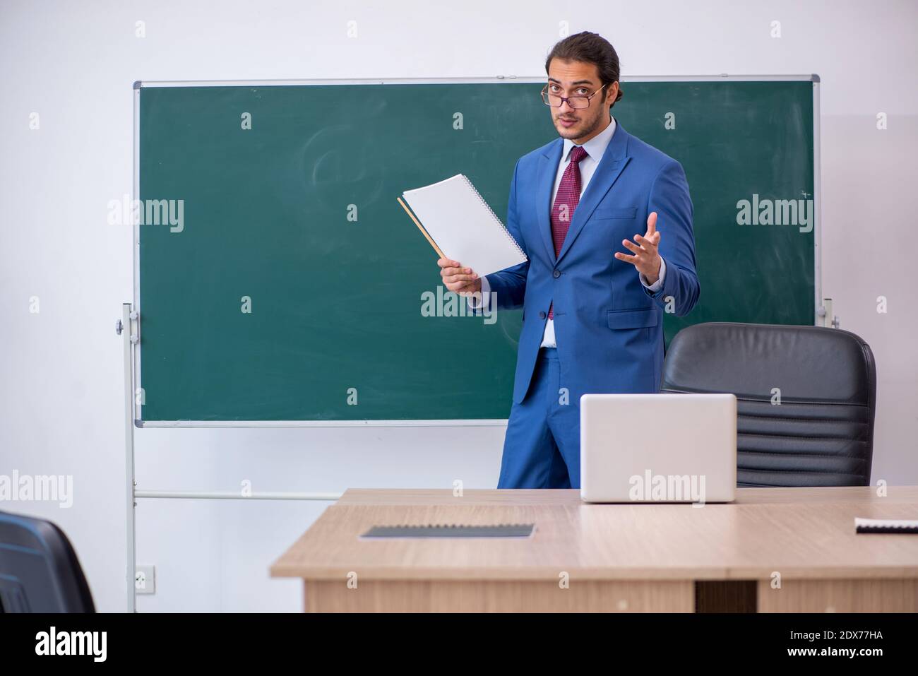 Young teacher in suit in front of green board Stock Photo - Alamy
