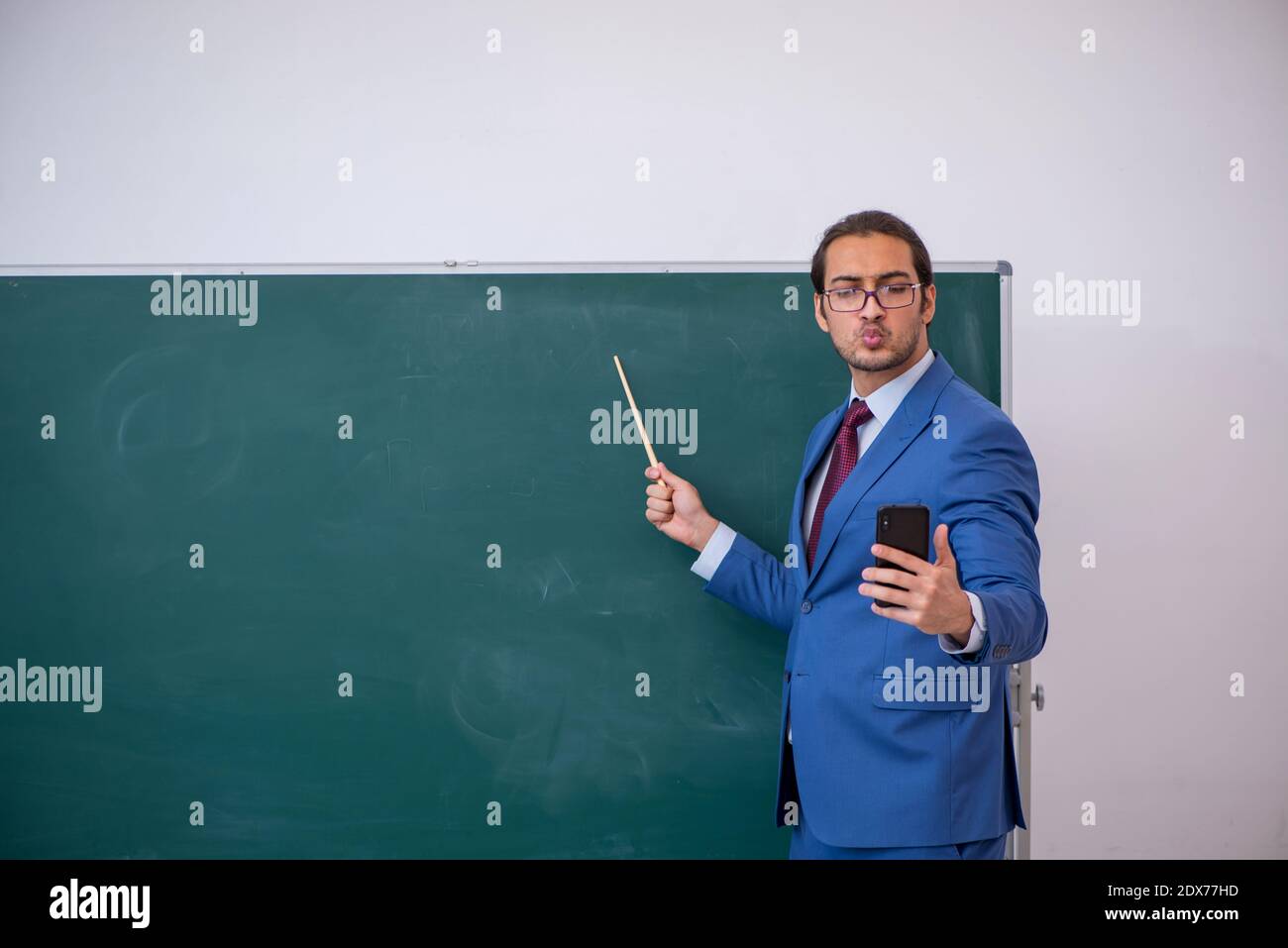 Young teacher in suit in front of green board Stock Photo - Alamy