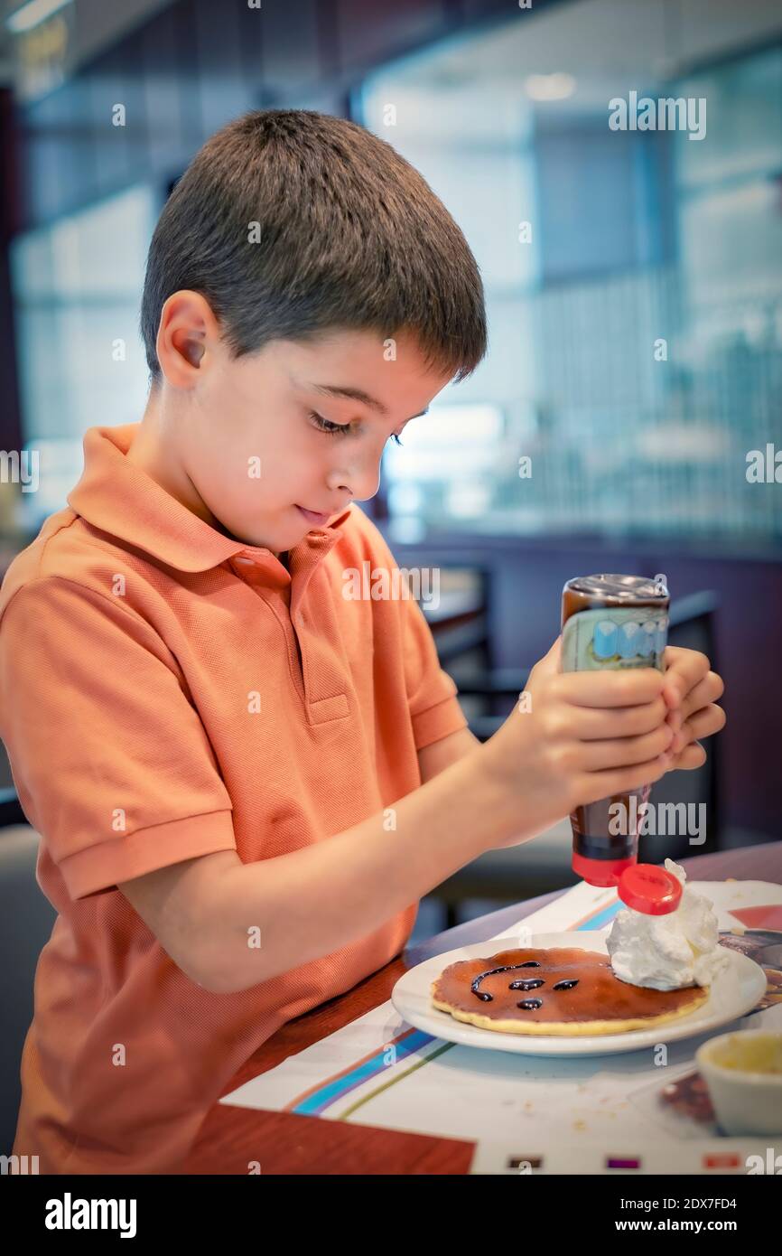 child decorates a pancake with chocolate syrup drawing a face with a ...