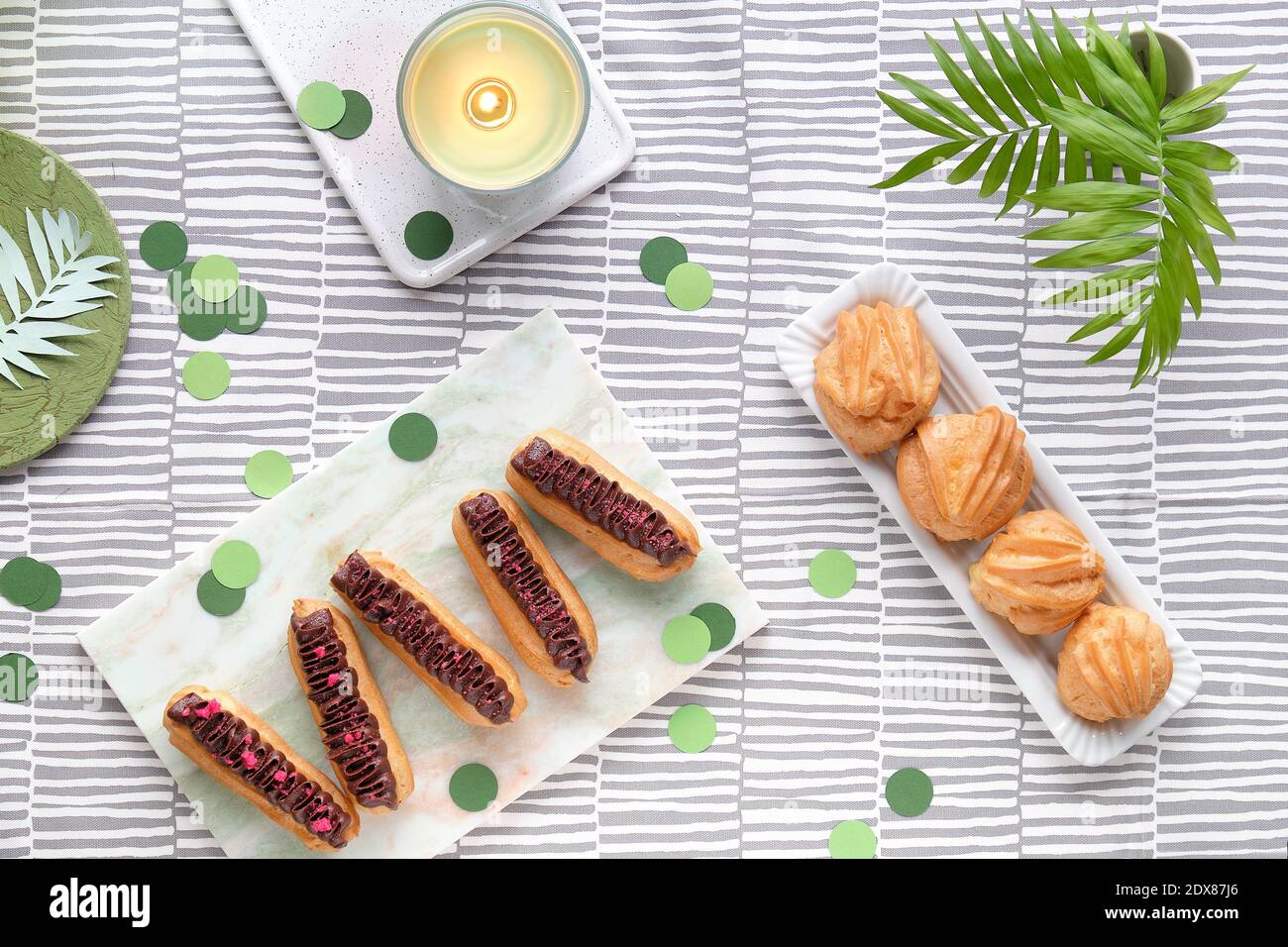Creative flat lay with exotic leaves. Assorted yummy eclairs, brewing ...