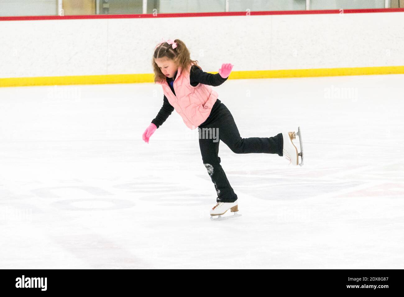 Little girl practicing figure skating moves on the indoor ice rink ...