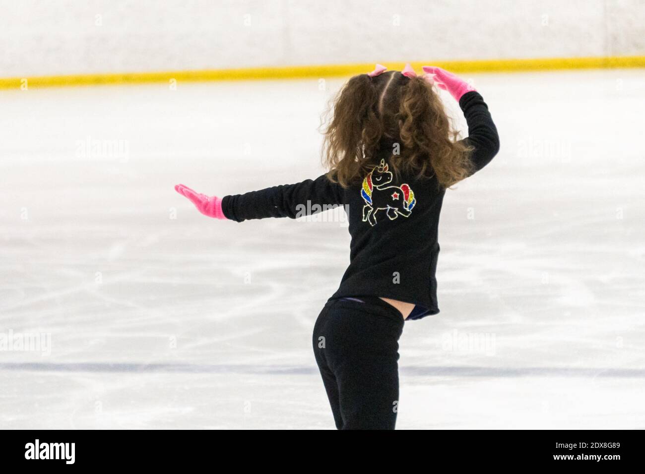 Little girl practicing figure skating moves on the indoor ice rink ...