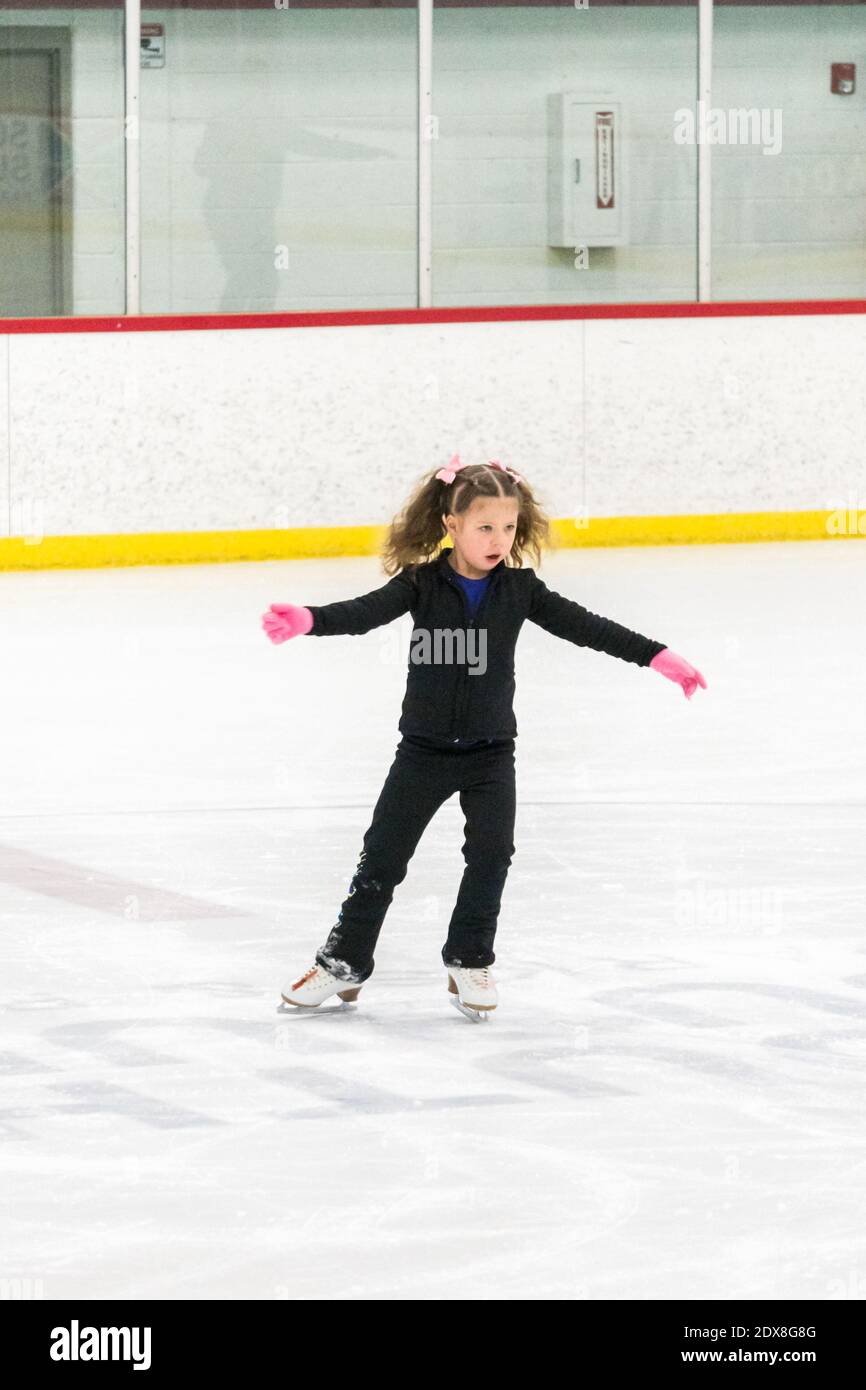 Little girl practicing figure skating moves on the indoor ice rink ...