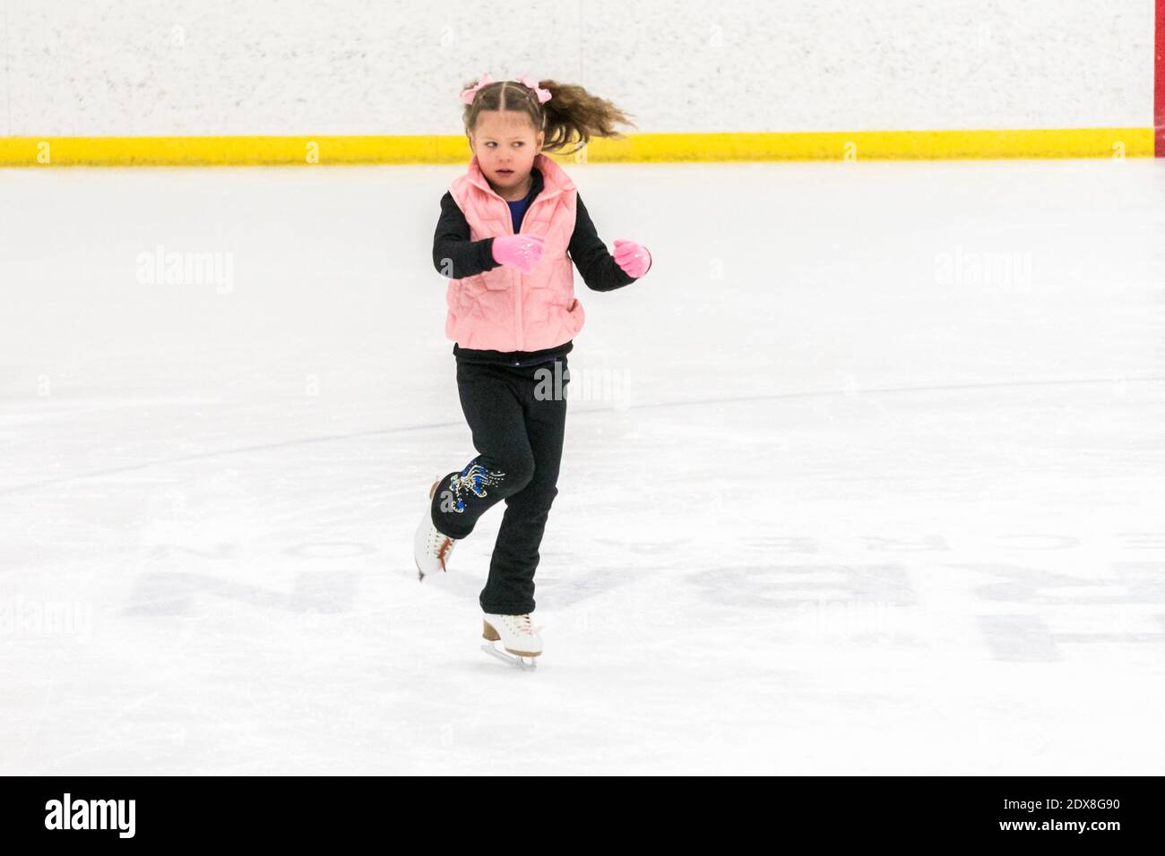 Little girl practicing figure skating moves on the indoor ice rink ...
