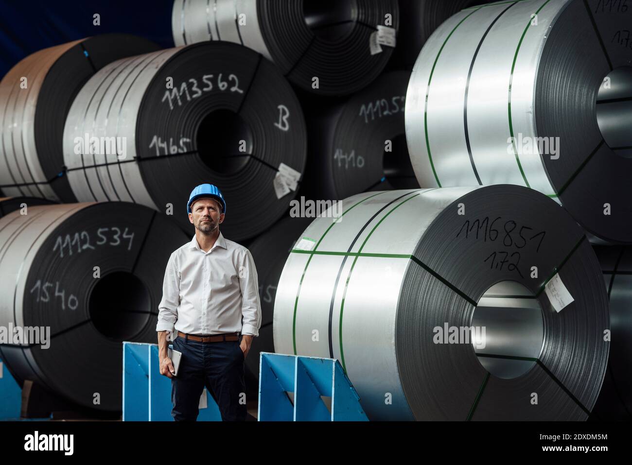 Male owner with hand in pocket standing against steel rolls in industry ...