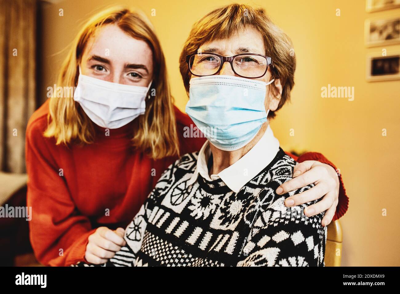 Granddaughter sitting with arm around on grandmother wearing face mask ...
