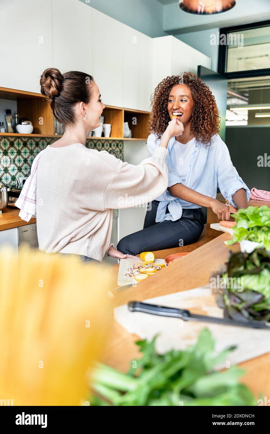 Businesswoman feeding vegetable to coworker while cooking together in ...