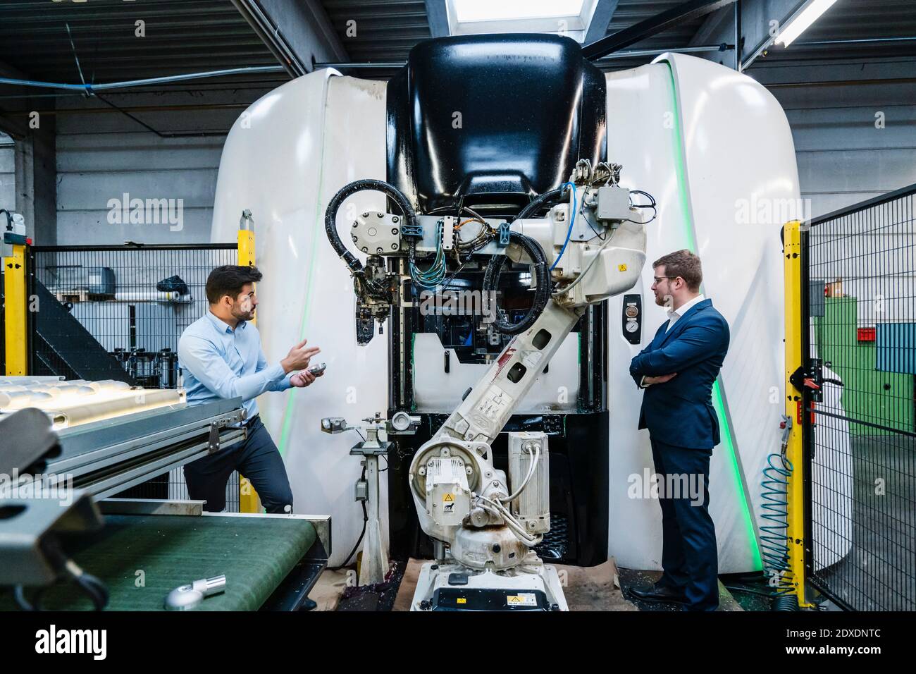 Businessman explaining male coworker about machinery while standing in ...
