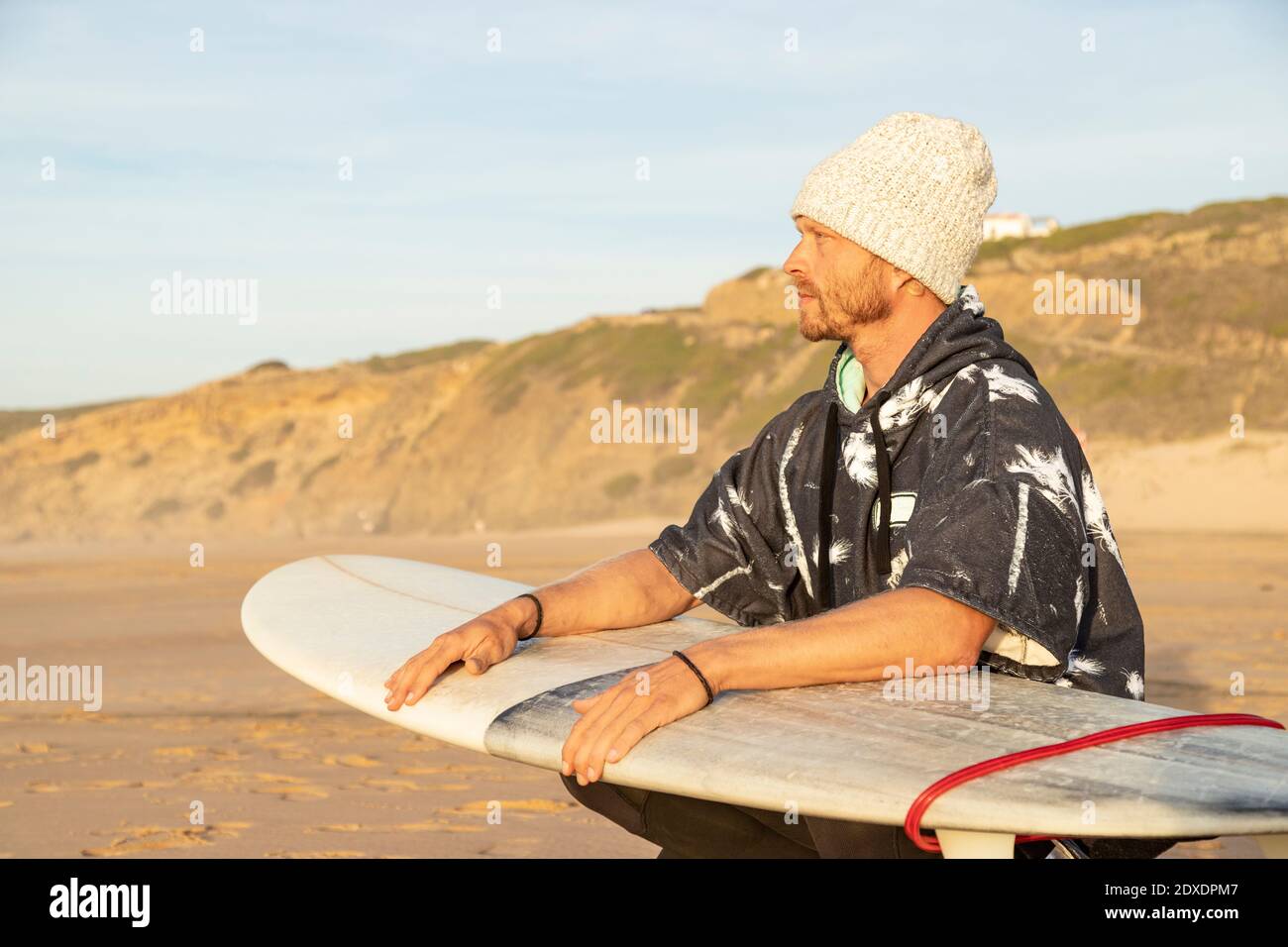 Man looking away while crouching with surfboard at beach Stock Photo ...
