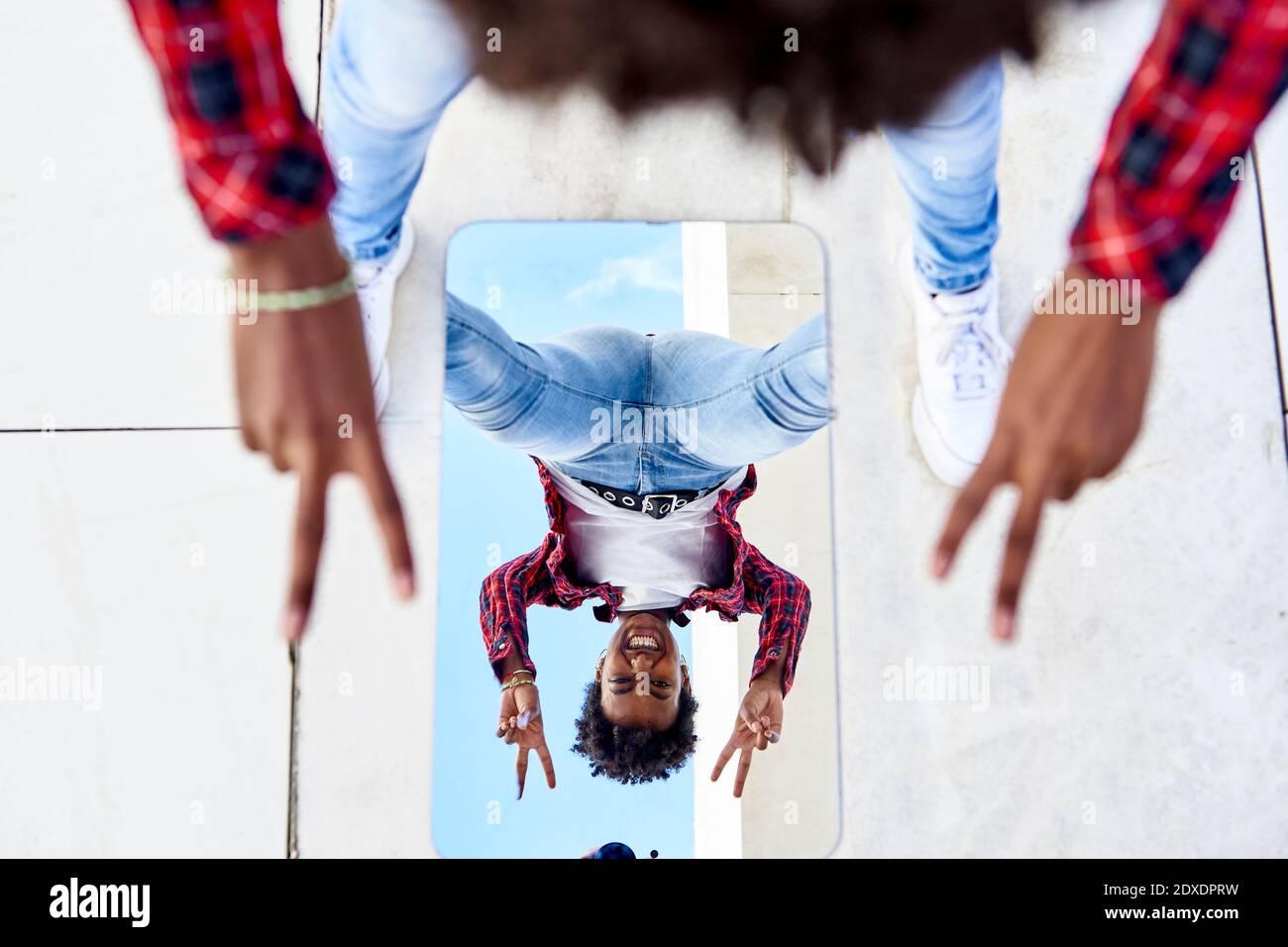 Playful young Afro woman showing peace sign to her mirror reflection ...