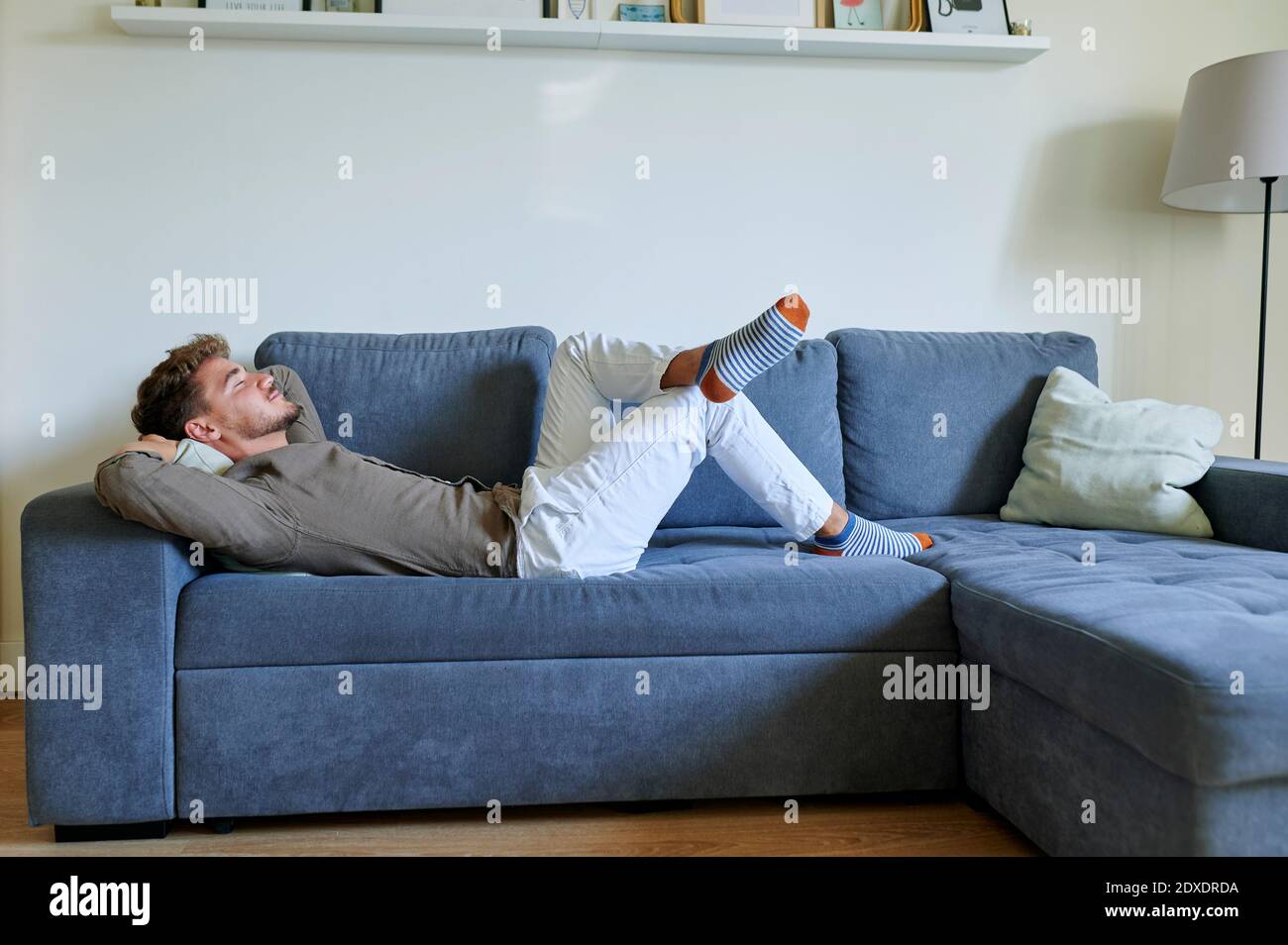 Man resting on sofa with hands behind head in living room at home Stock ...