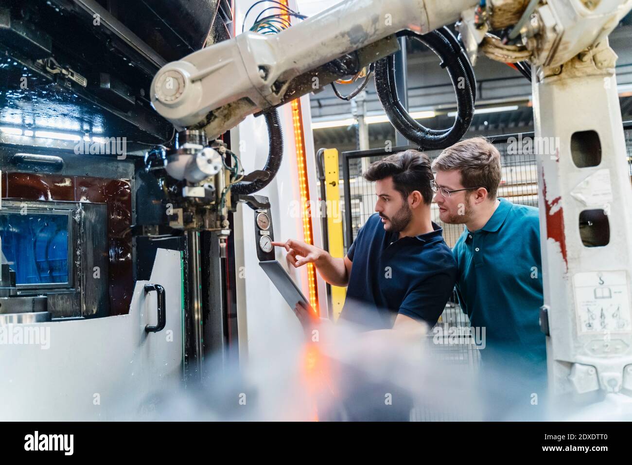 Male coworkers using digital tablet while examining robotic arm at ...