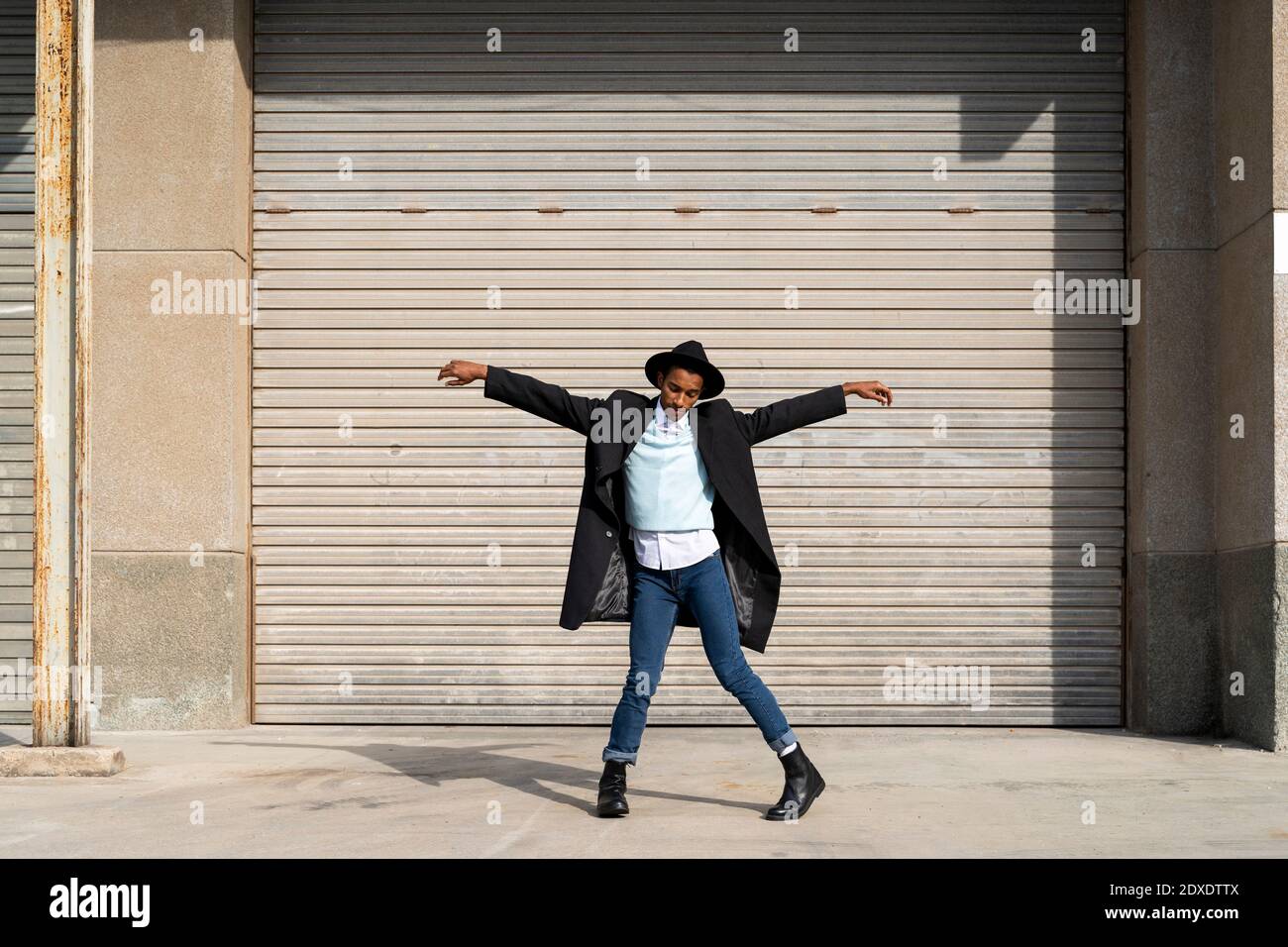 Fashionable young man dancing with arms outstretched against shutter ...