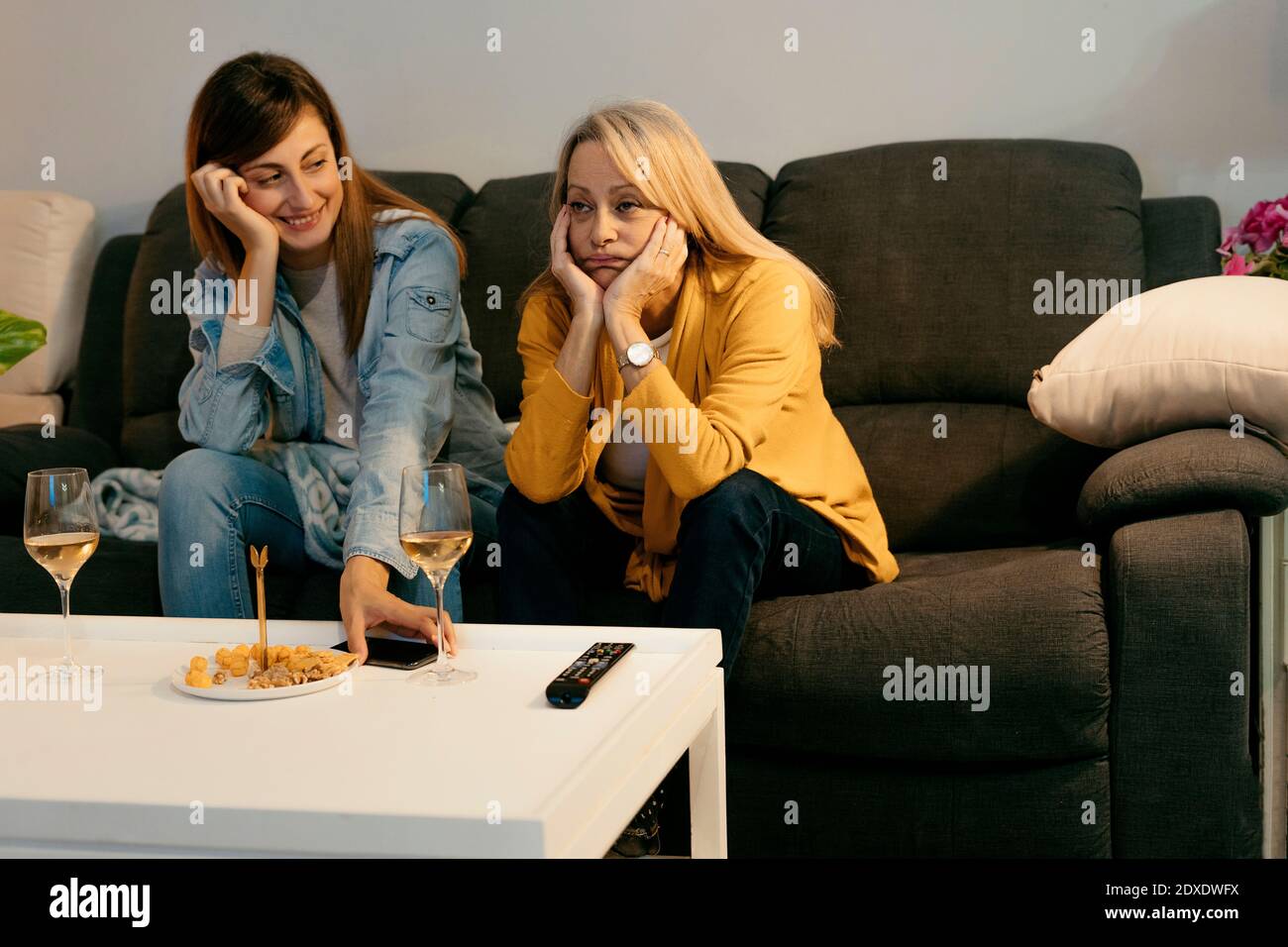 Bored mother holding face while sitting next to smiling daughter on ...