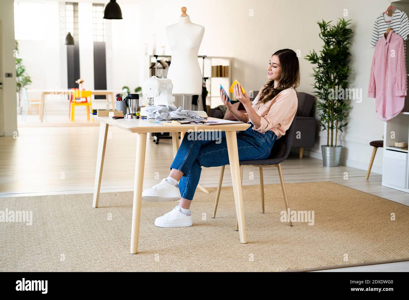 Female tailor examining fabric swatches while sitting on chair in ...