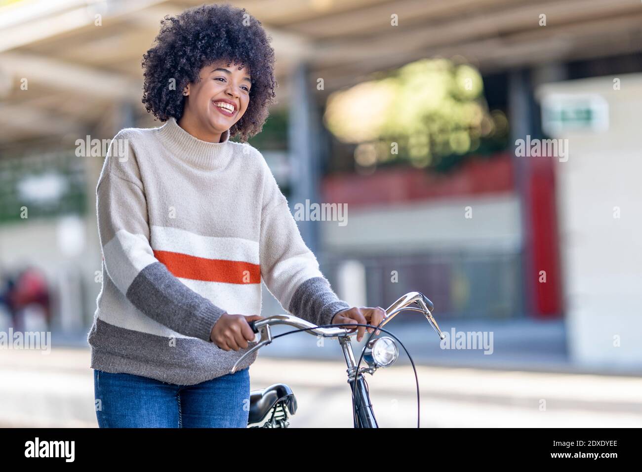 Cheerful young woman wheeling bicycle while looking away at railroad ...