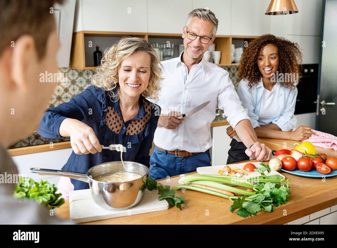 Mature businesswoman cooking spaghetti with coworkers in office kitchen ...