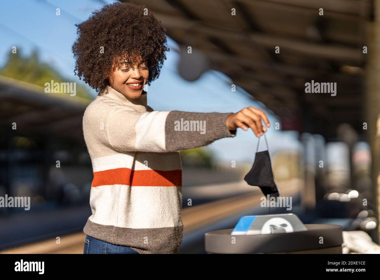 Young woman throwing used protective face mask in garbage bin at ...