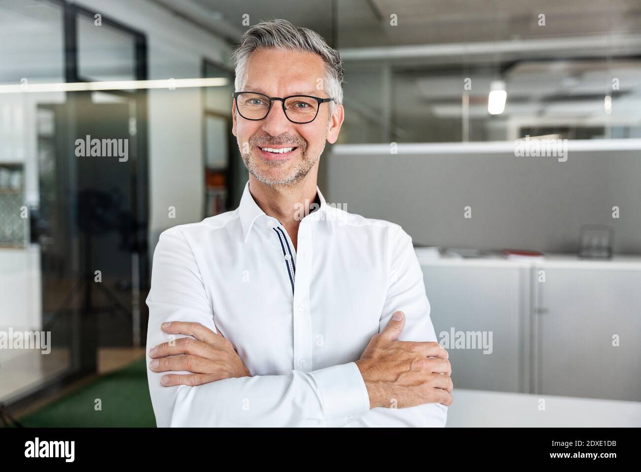 Happy male entrepreneur with arms crossed at work place Stock Photo - Alamy