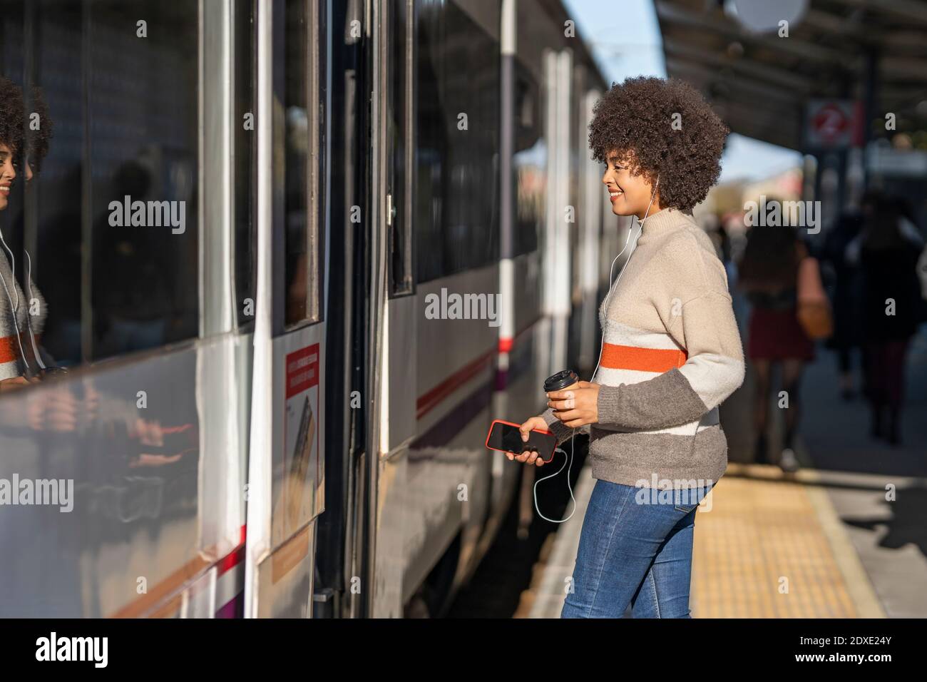 Happy young female passenger boarding train at station on sunny day ...