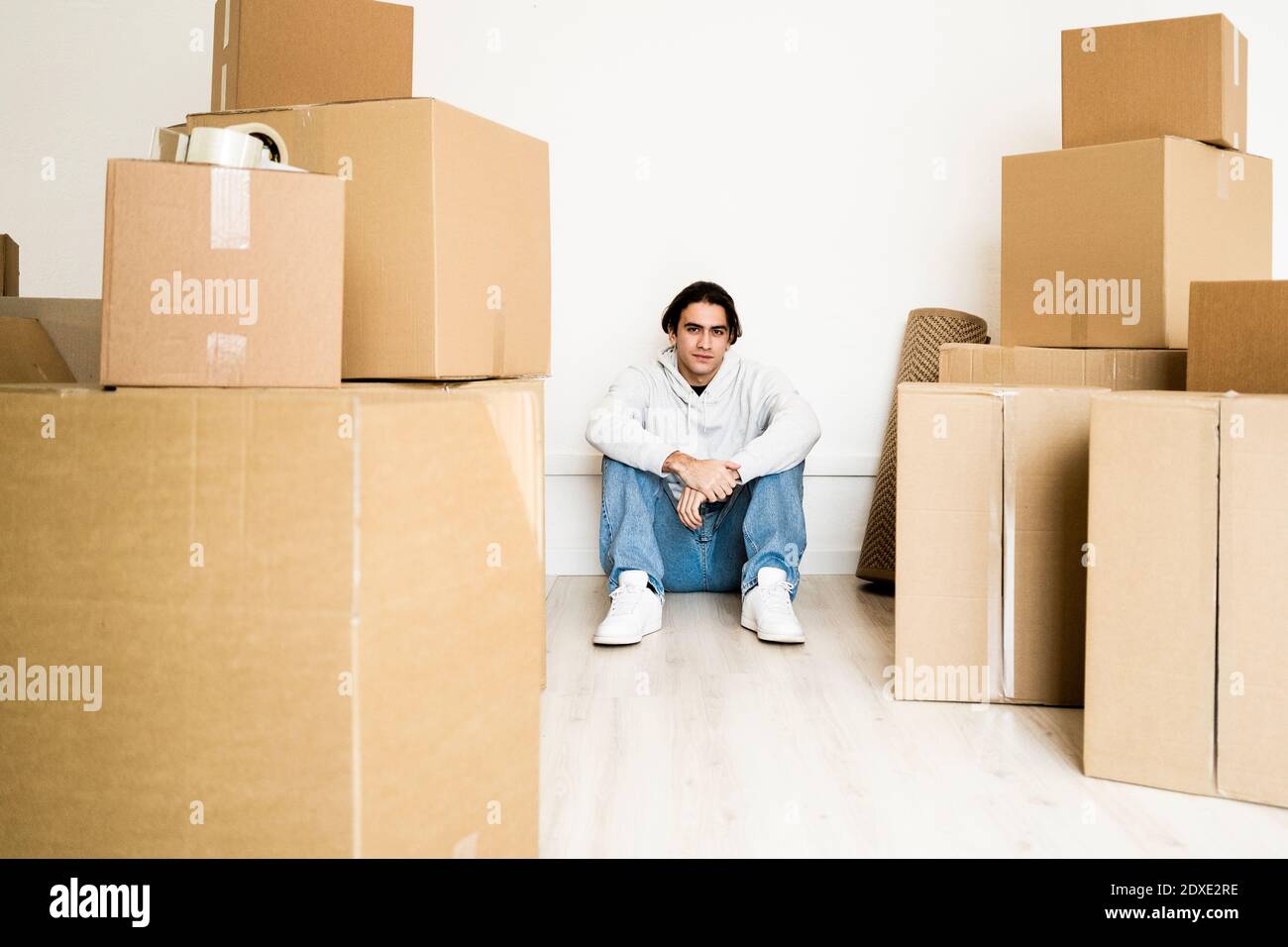 Man sitting amidst cardboard boxes on floor in living room of new house ...
