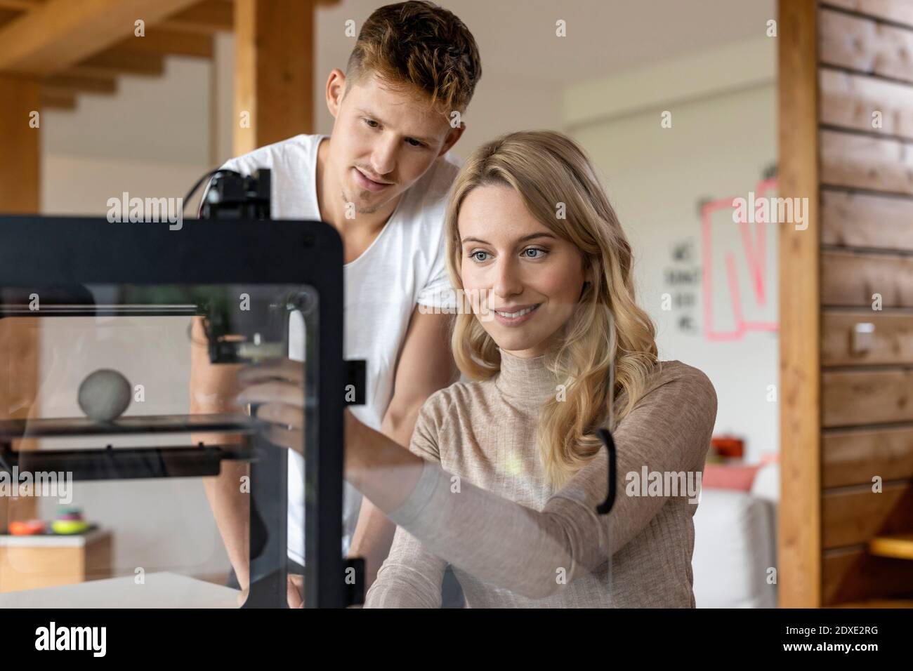Businesswoman operating 3D printer while sitting at home by colleague ...