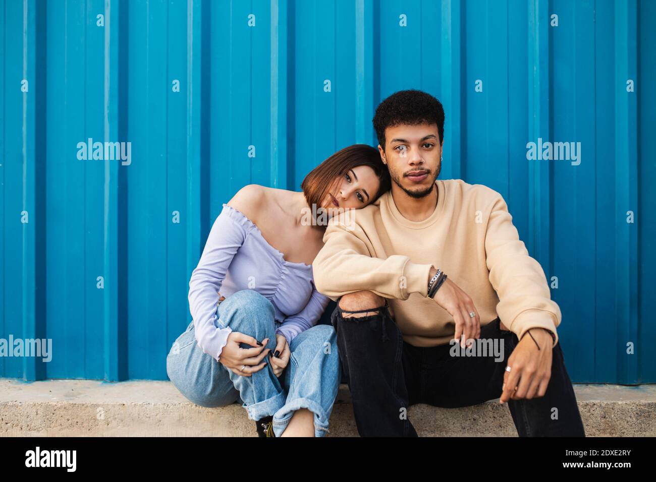 Girlfriend leaning on boyfriend's shoulder while sitting against blue ...