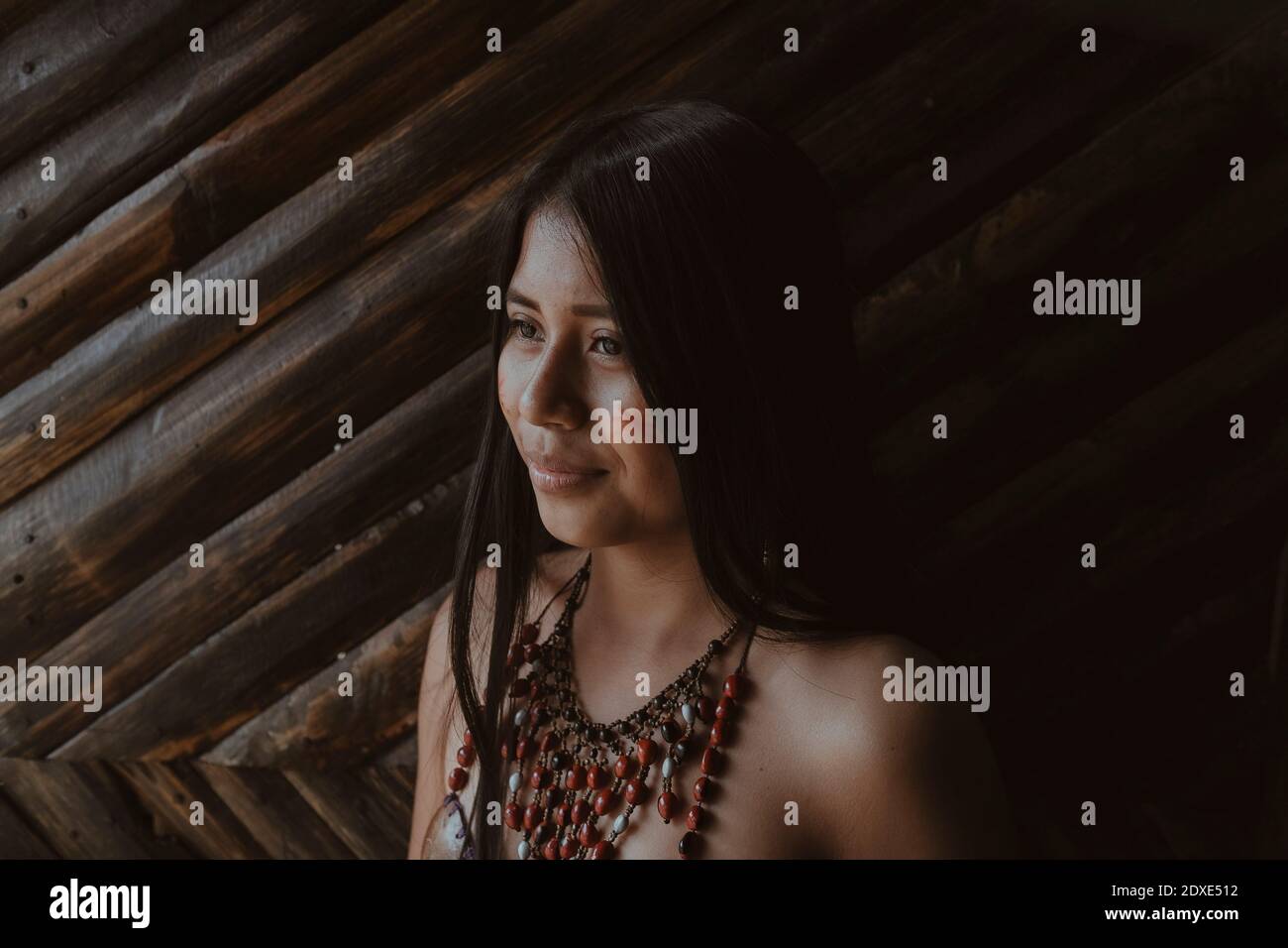 Thoughtful young Guarani woman looking away against bamboo wall ...