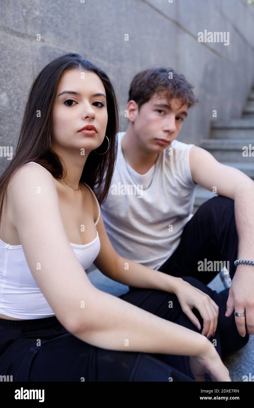 Young man and woman staring while sitting on staircase Stock Photo - Alamy